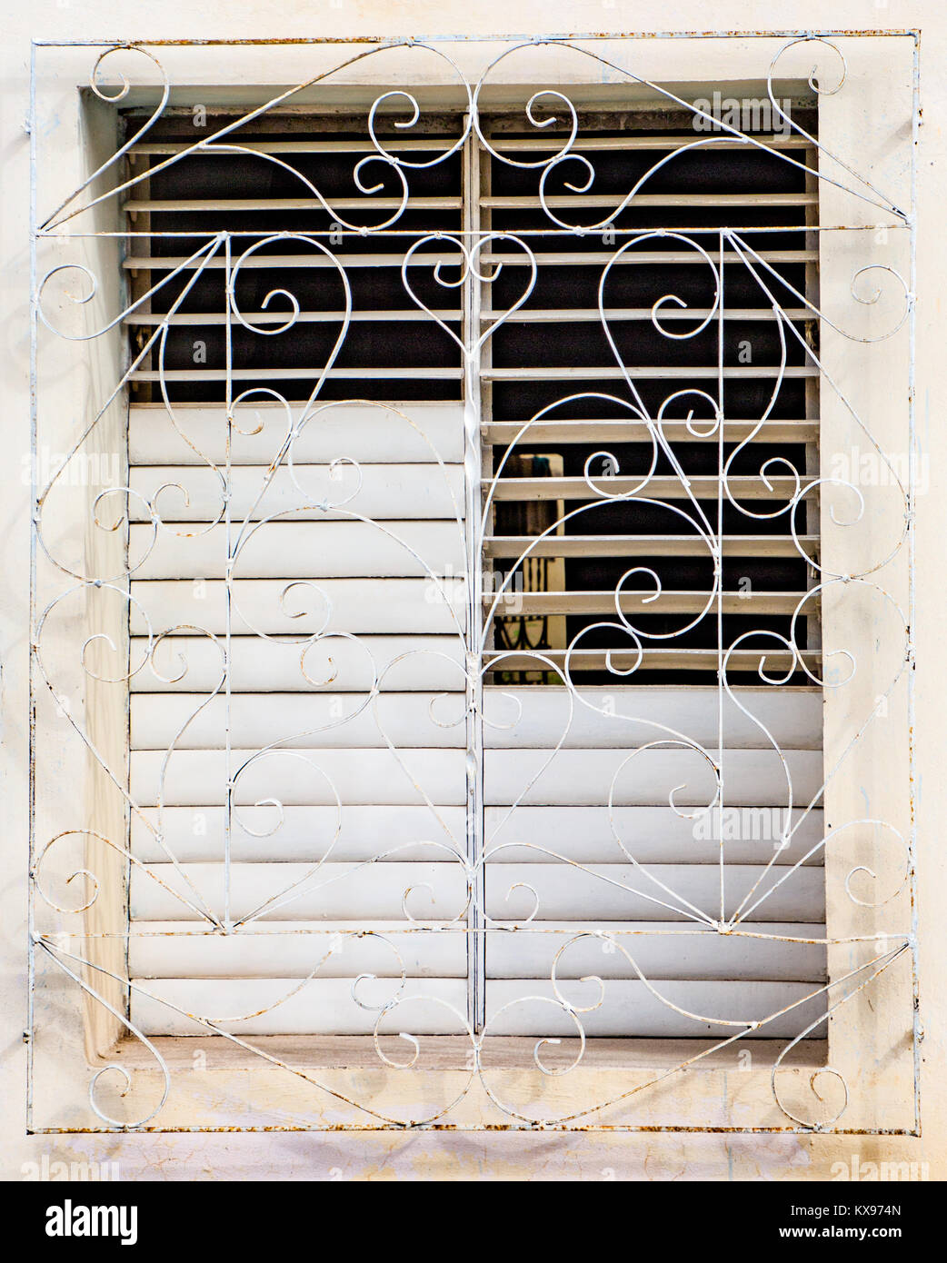 Partially open white shutters on window behind white fancy metal grill ...