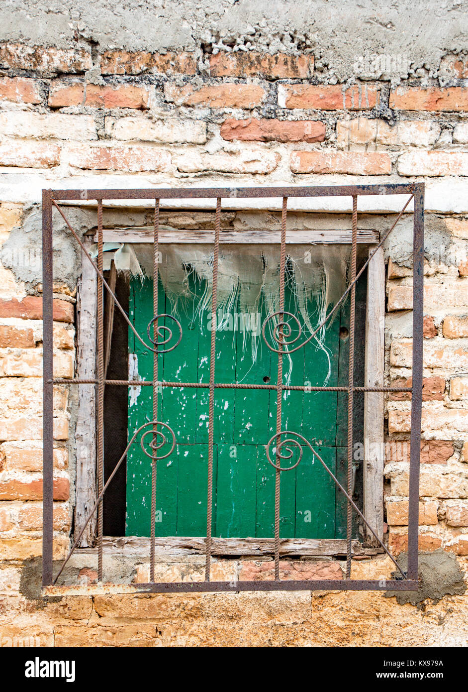 Green shutters block window behind rusted grill on unfinished brick ...