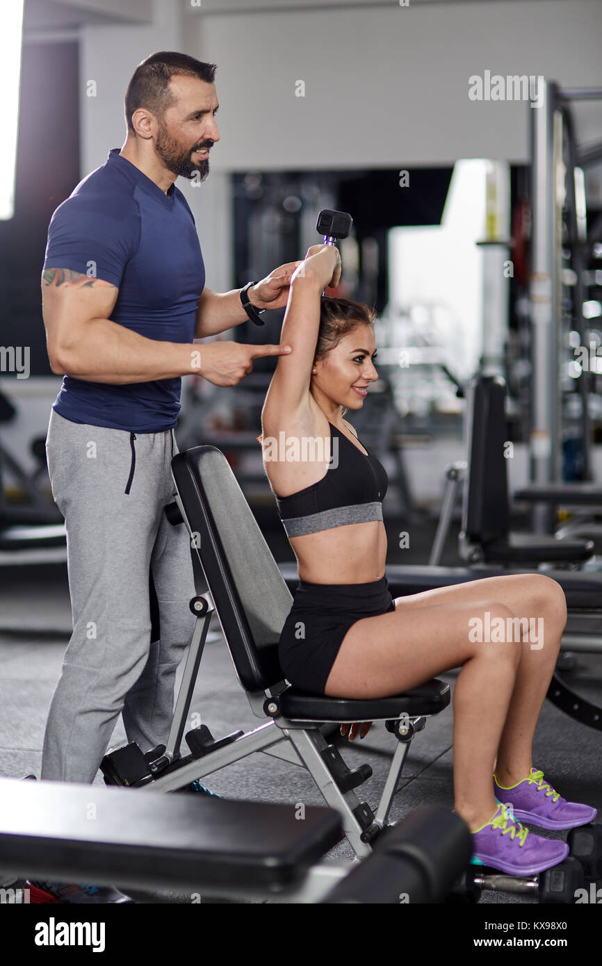 Personal Trainer Helping Woman With Triceps Workout In The Gym Stock
