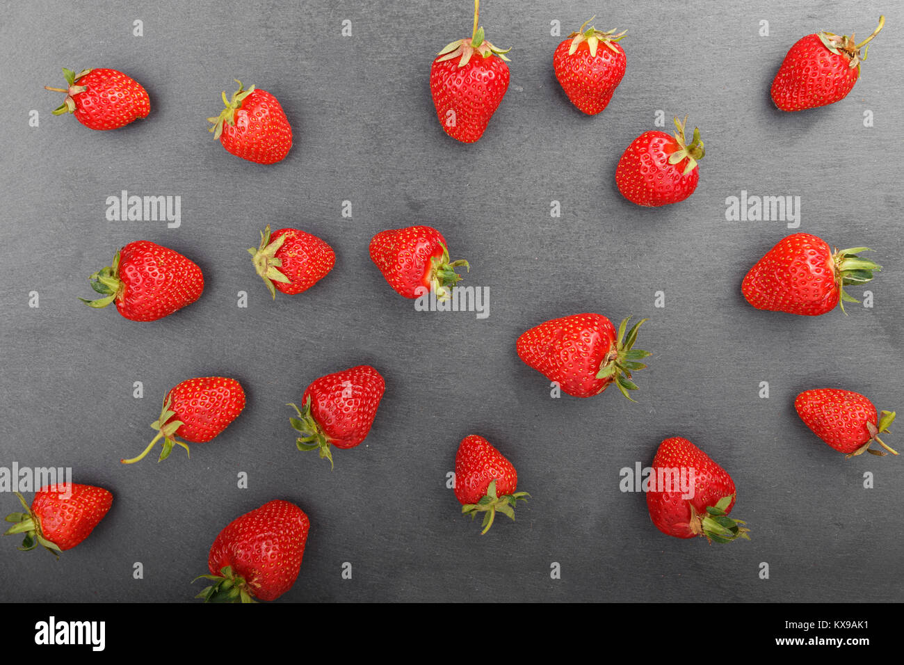 A ripe strawberry is scattered on the black background of a slate board ...