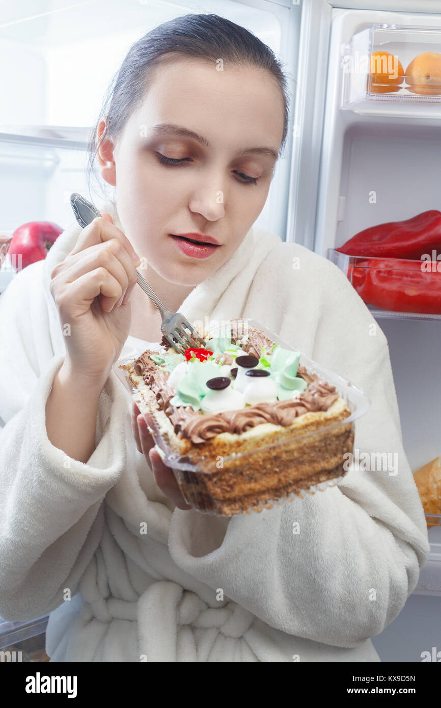 sad woman eating sweet cake near refrigerator Stock Photo - Alamy