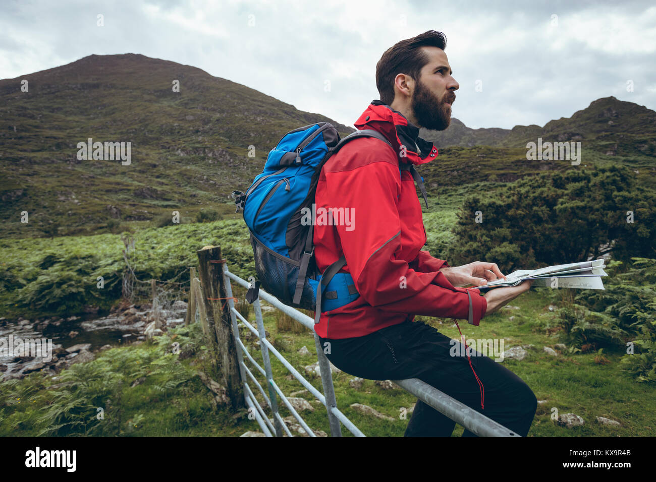 Male hiker sitting sitting on the fence with a map Stock Photo - Alamy