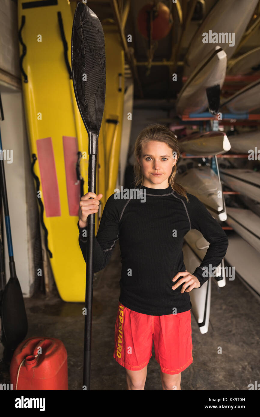 Life guard standing one hand on waist and other hand holding paddle ...