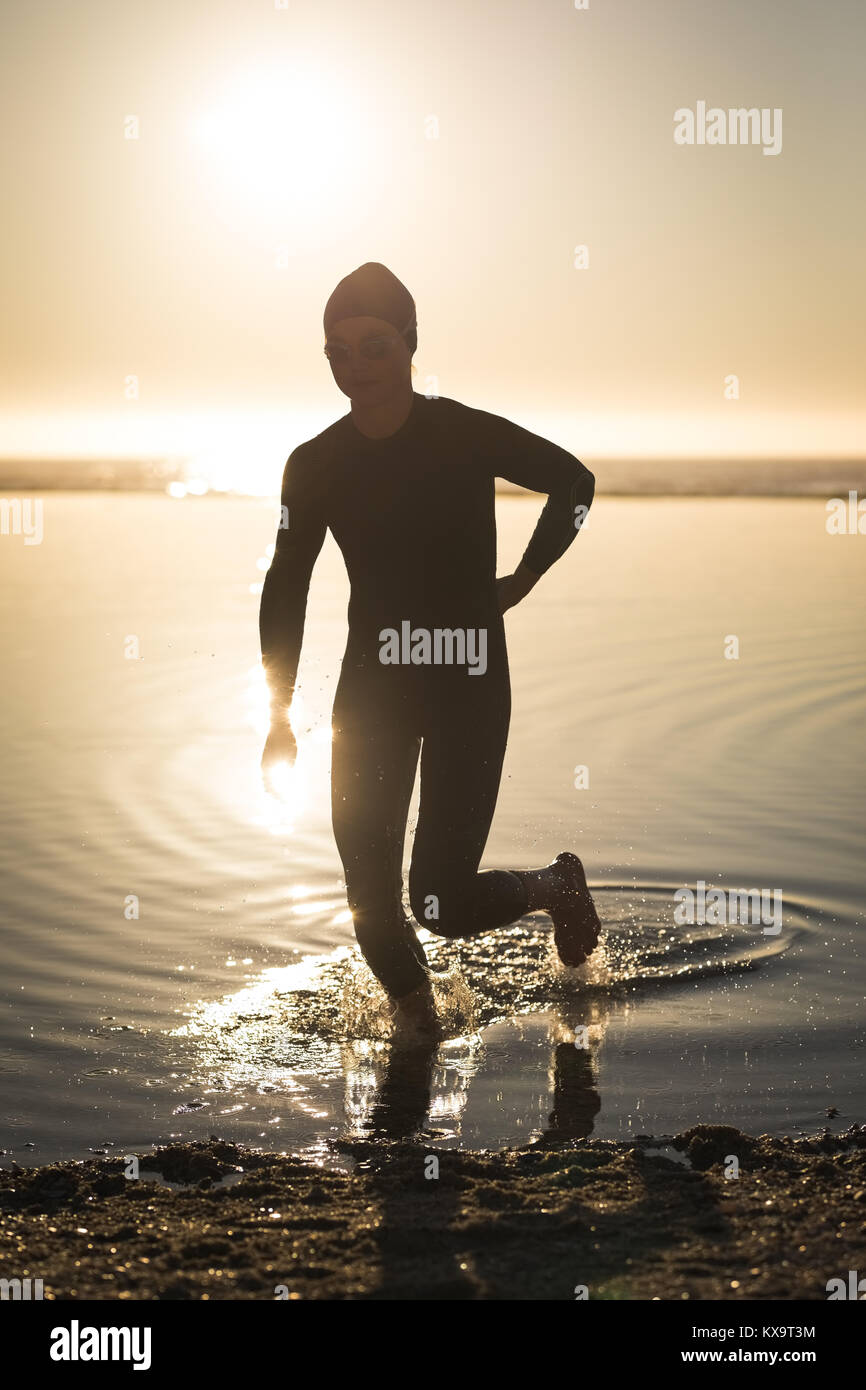 Woman in wetsuit running in shallow water Stock Photo - Alamy