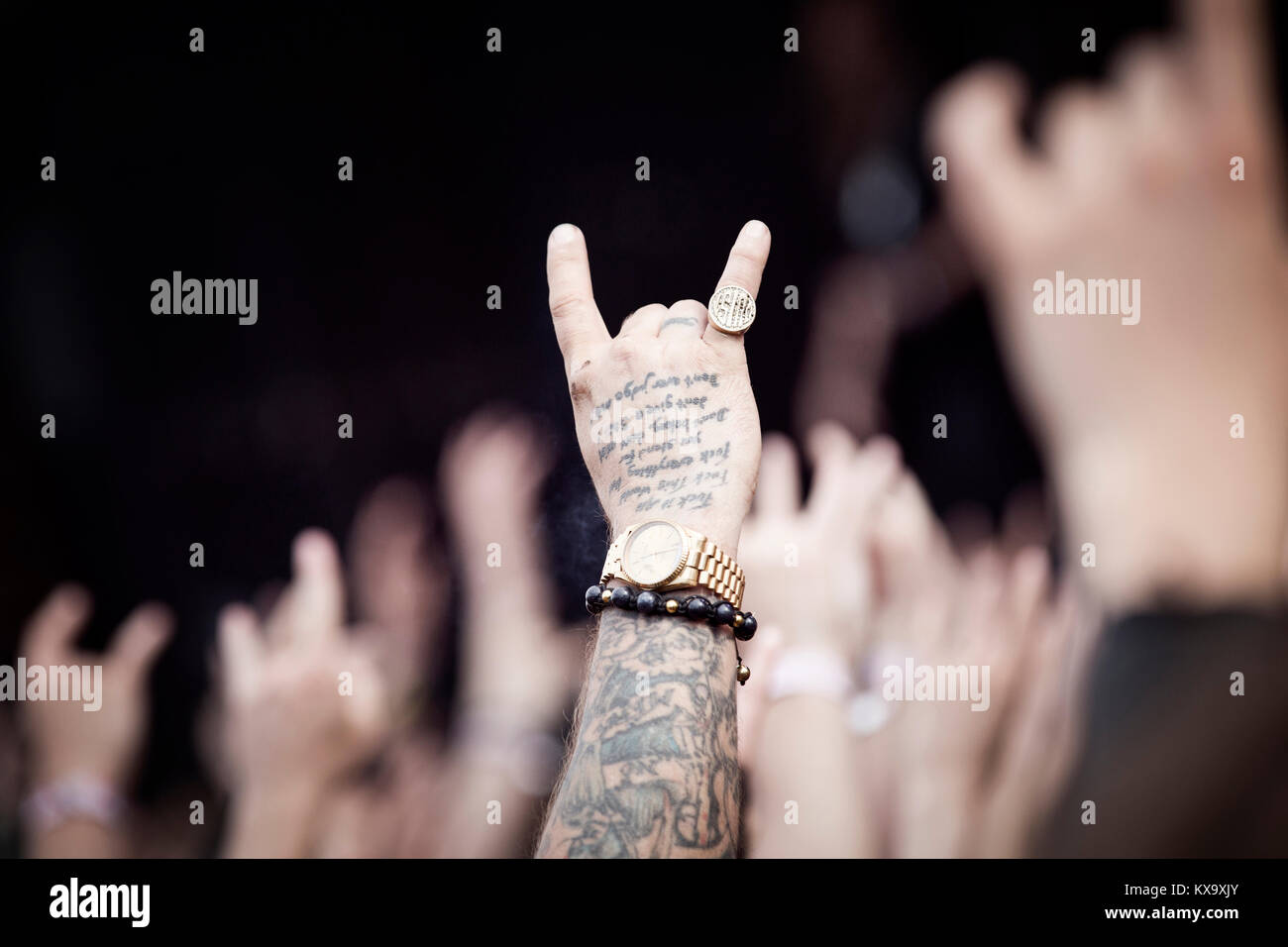 A heavy metal fan with a tattoed arm and hand is showing the Sign of ...