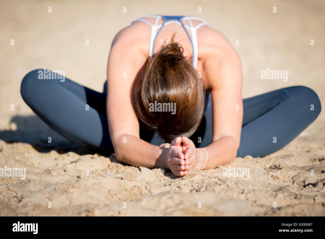 Woman practicing yoga in the sand - Bound Angle Pose Forward - Baddha ...