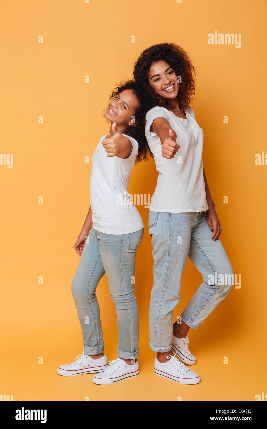 Full length portrait of two happy african sisters standing back to back ...