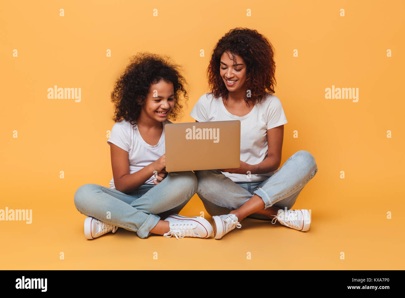 Two smiling afro american sisters using laptop computer while sitting ...
