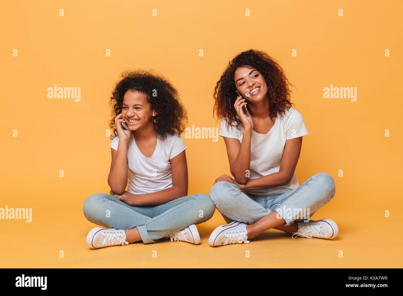 Portrait of a two cheerful afro american sisters talking on mobile ...