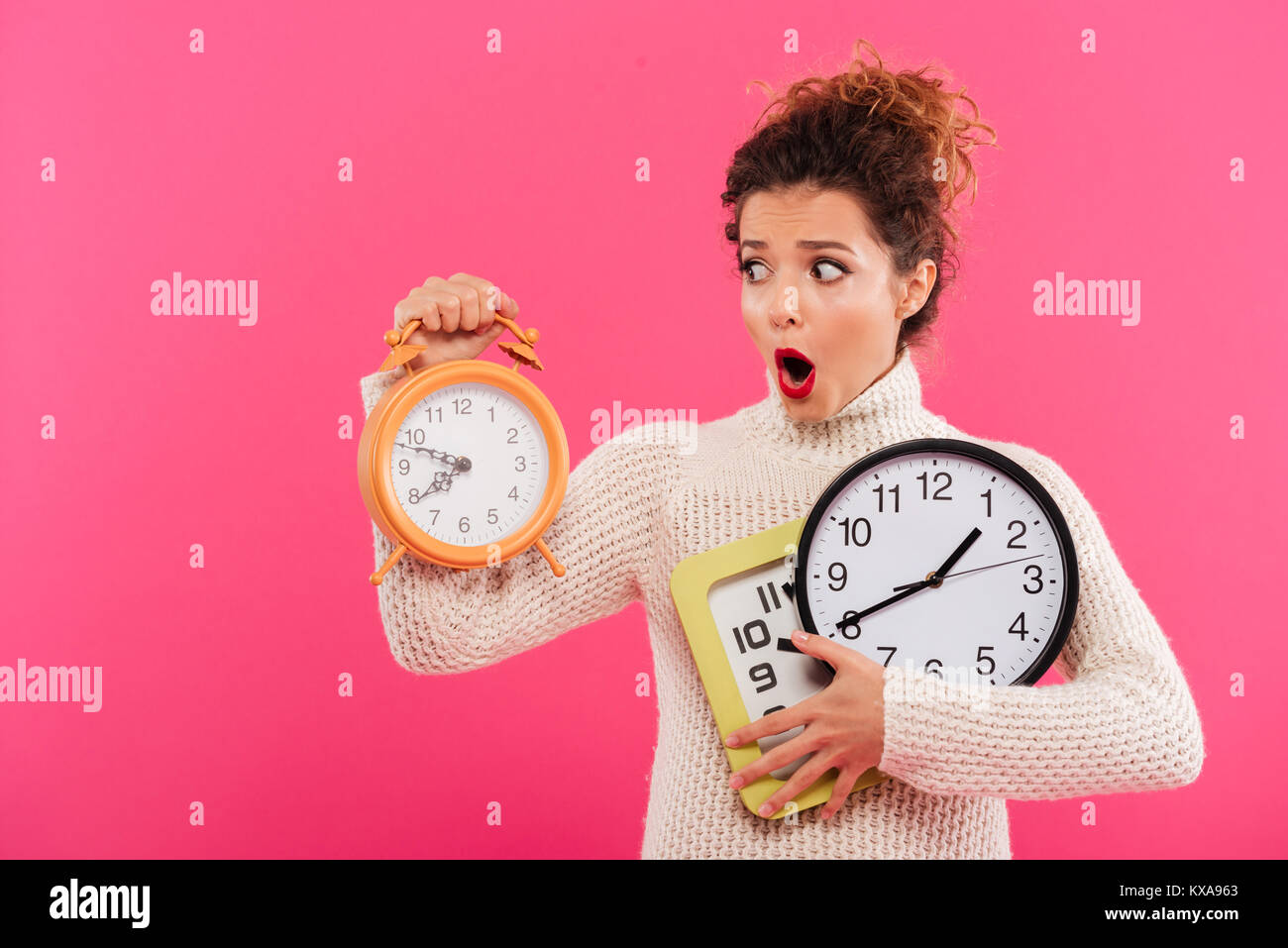 Portrait of a shocked pretty woman holding alarm clocks isolated over ...