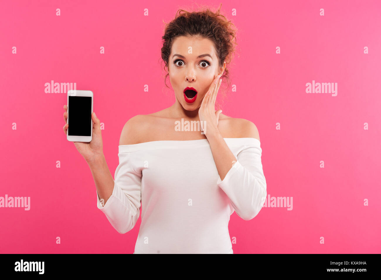 Portrait of a shocked pretty girl showing blank screen mobile phone ...
