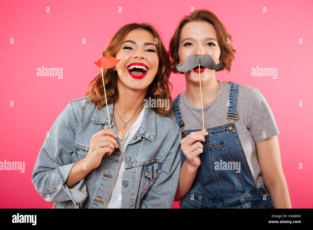 Photo of two funny women friends standing isolated over pink background ...