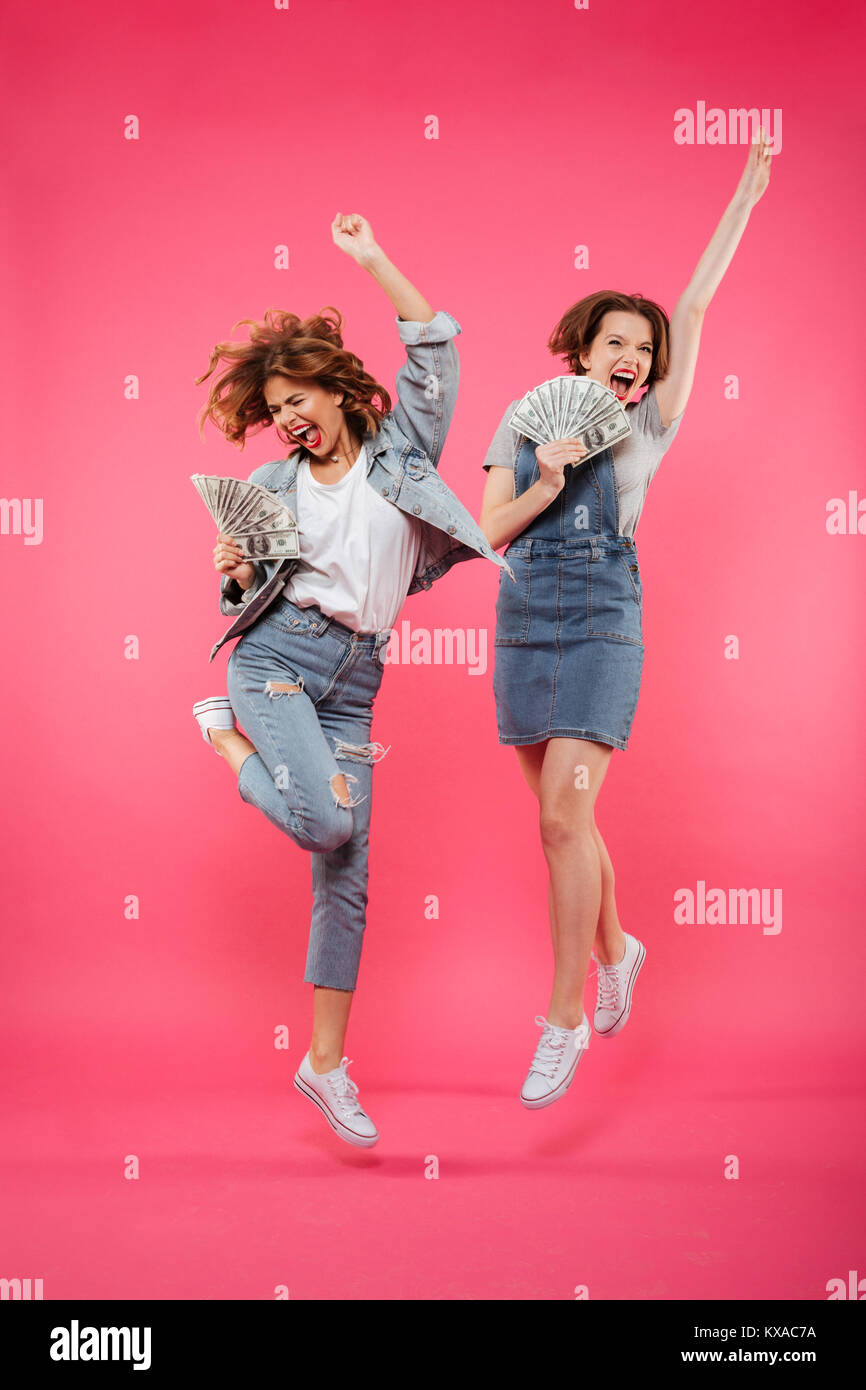 Image Of Screaming Pretty Two Women Friends Holding Money Jumping Isolated Over Pink Background