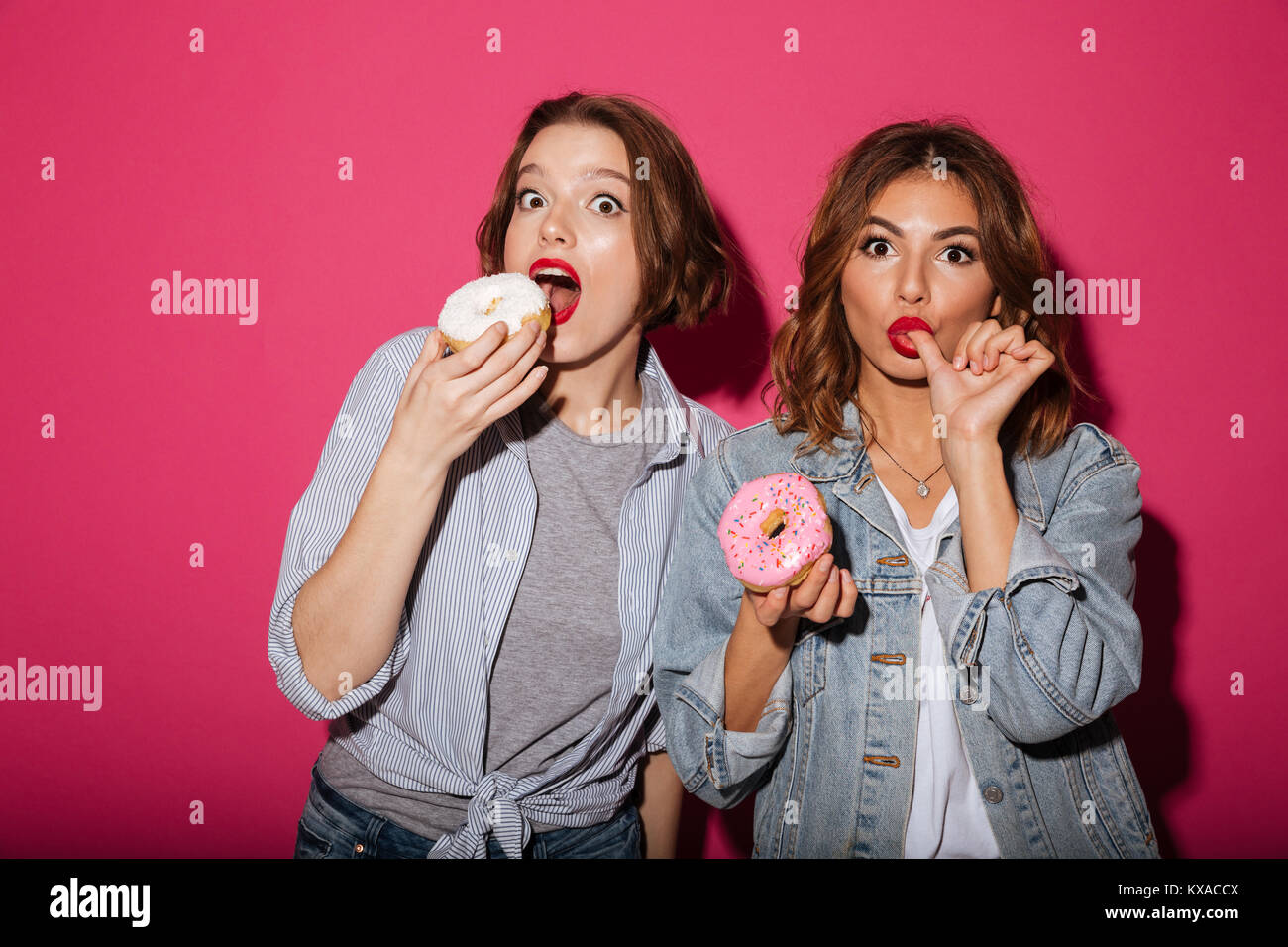 Picture of amazing two women friends eating donuts isolated over pink ...