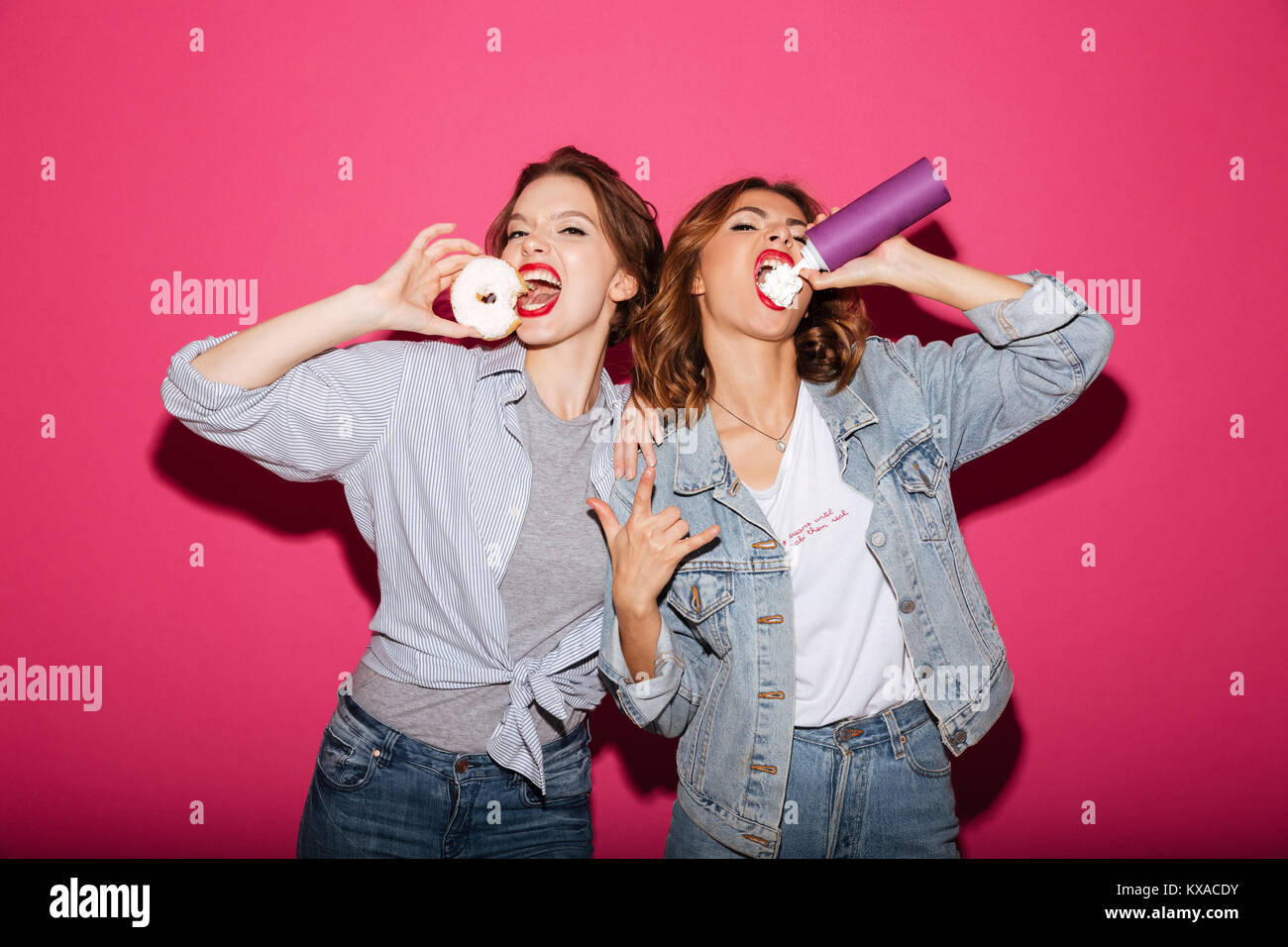 Picture of amazing two women friends eating sweeties isolated over pink ...