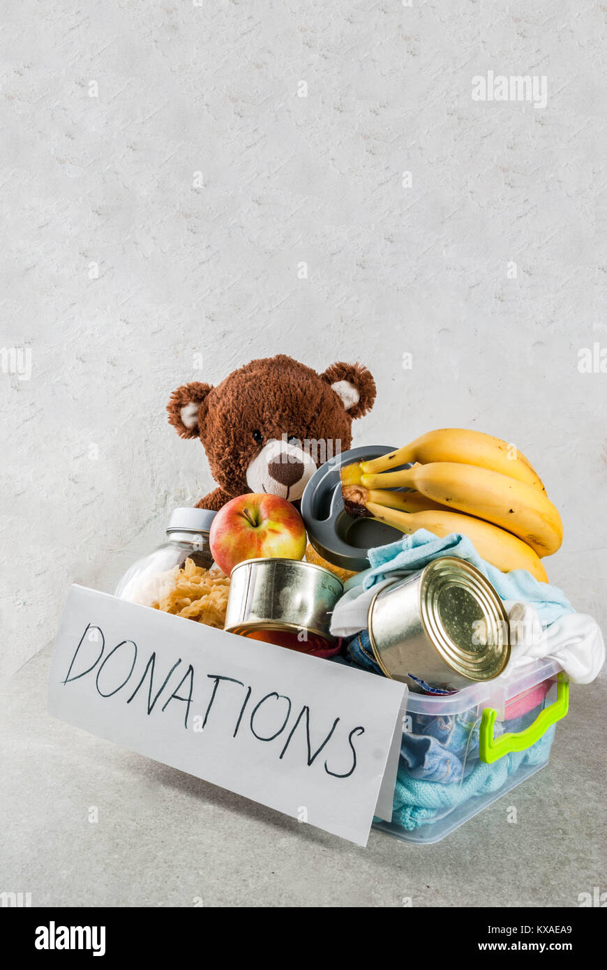 Plastic donation box with toys, clothes and food, white grey background ...