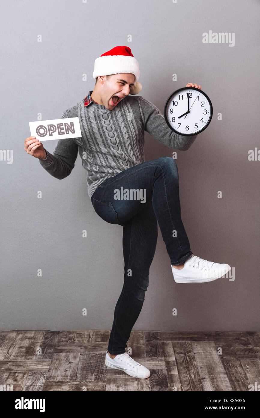 Full length image of happy man in sweater and christmas hat holding ...