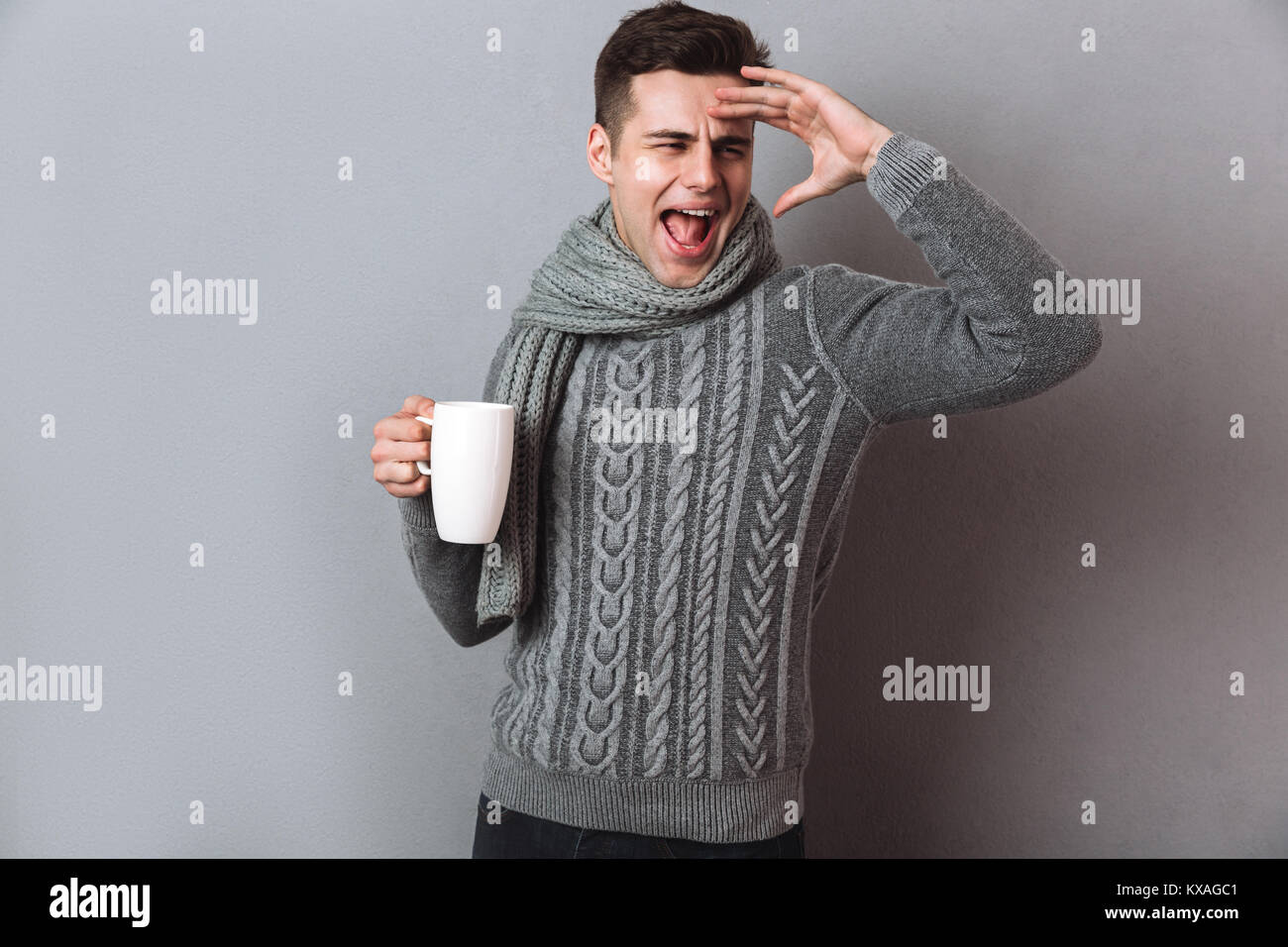 Happy Sick Man in sweater and scarf holding cup of tea and looking away ...