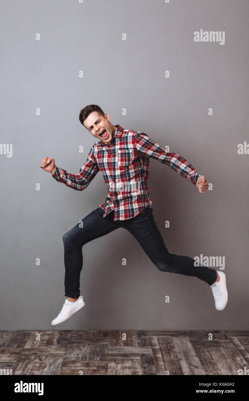 Full length image of happy man in shirt and jeans screaming while ...
