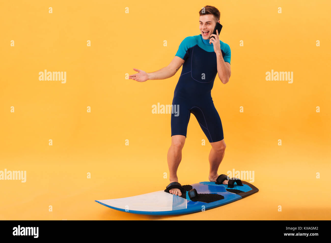 Image of Surprised happy surfer in wetsuit using surfboard and talking ...
