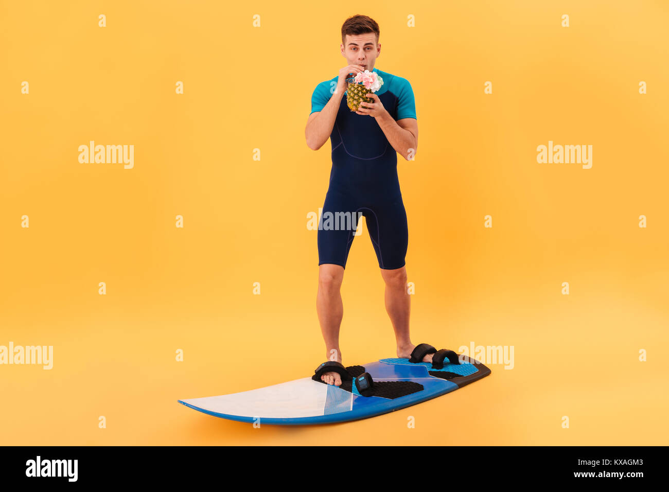 Image of Smiling surfer in wetsuit using surfboard while drinking ...