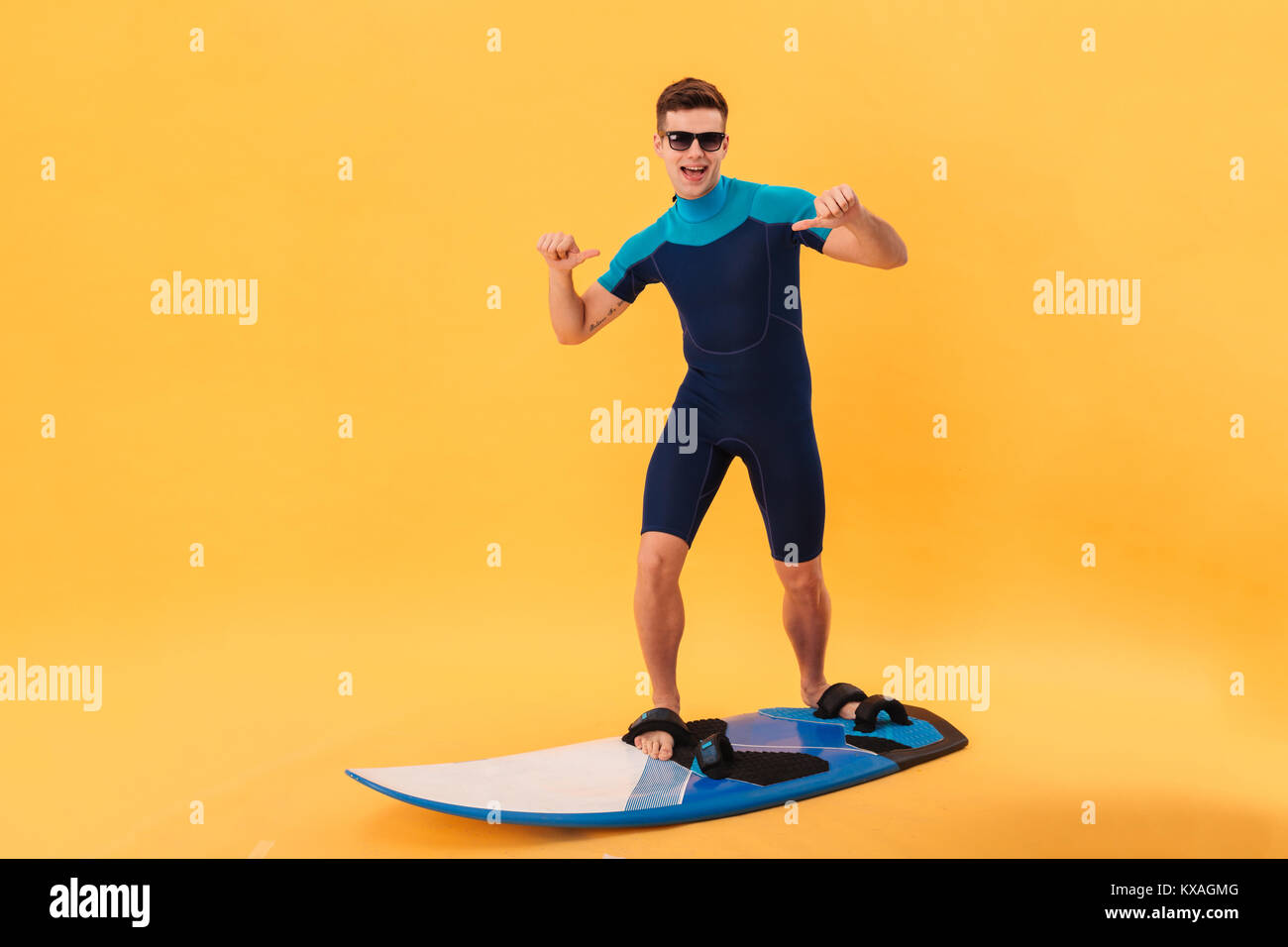Cheerful surfer in wetsuit and sunglasses using surfboard indicates ...
