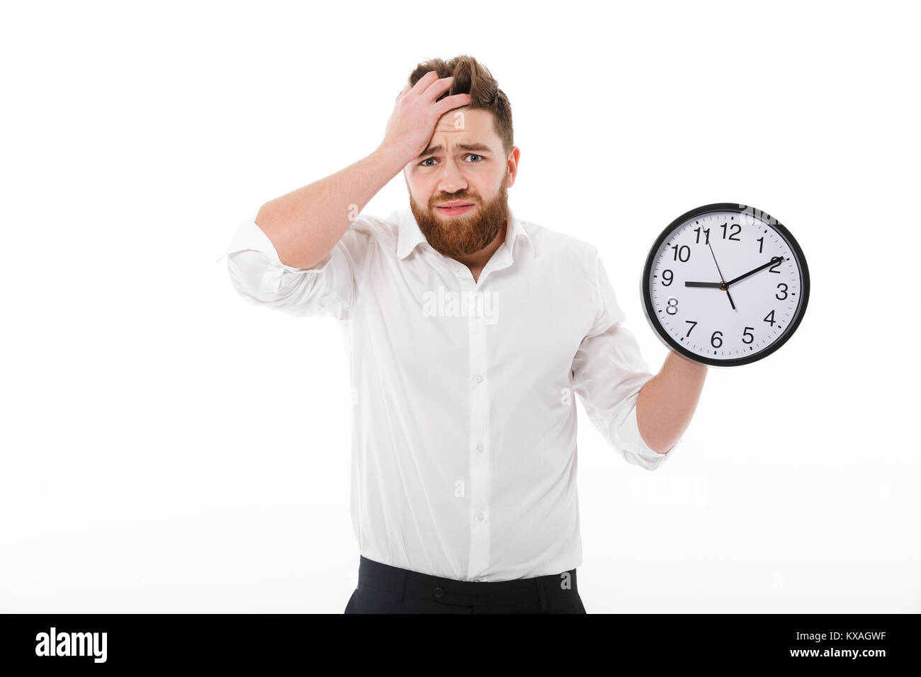 Confused bearded man in business clothes holding clock and looking at ...