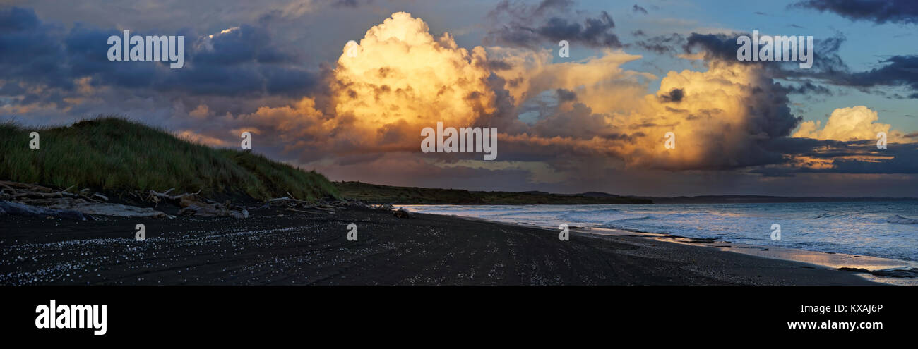 Sunset at the dark sandy beach, big clouds illuminated by the sun ...