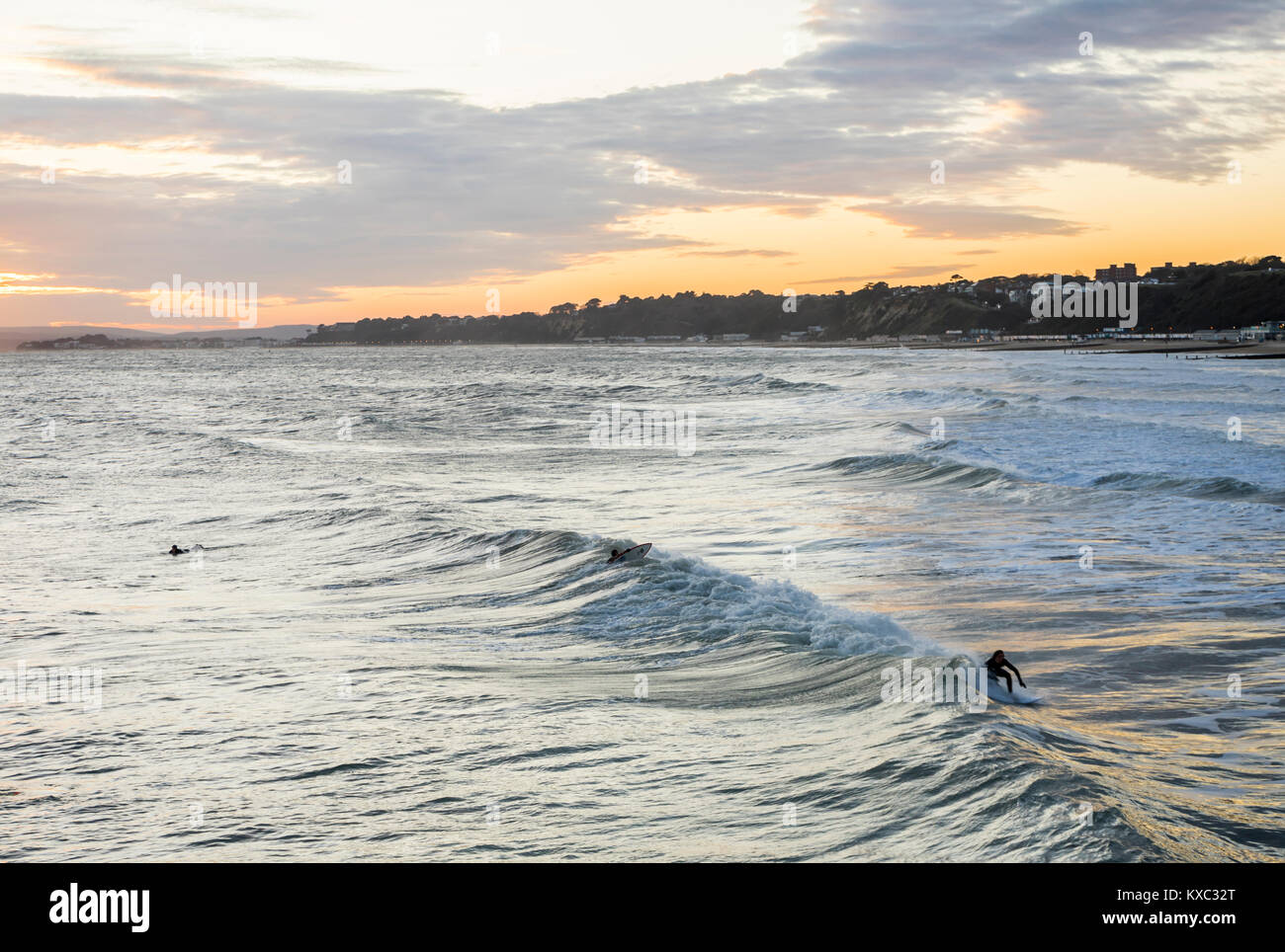 Golden sunset over Bournemouth seafront/ seaside with surfers enjoying ...