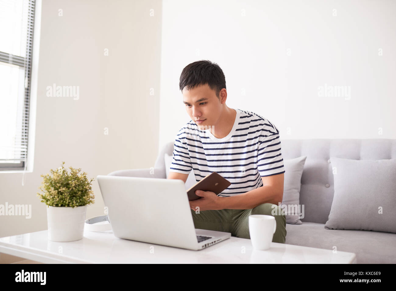 Handsome serious man, looking at laptop screen and writing something in ...