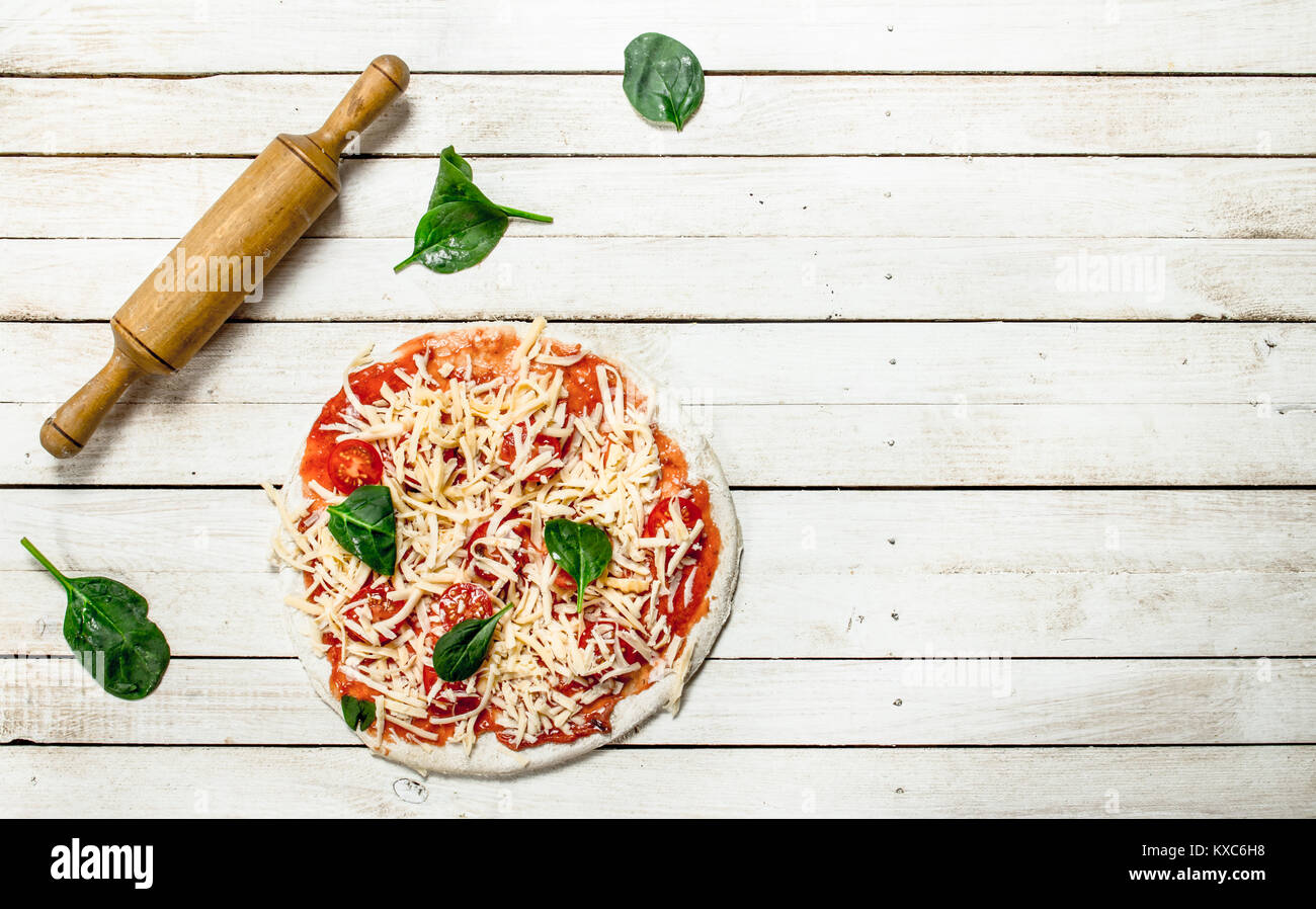 Preparation of pizza with various ingredients. On a white wooden table ...