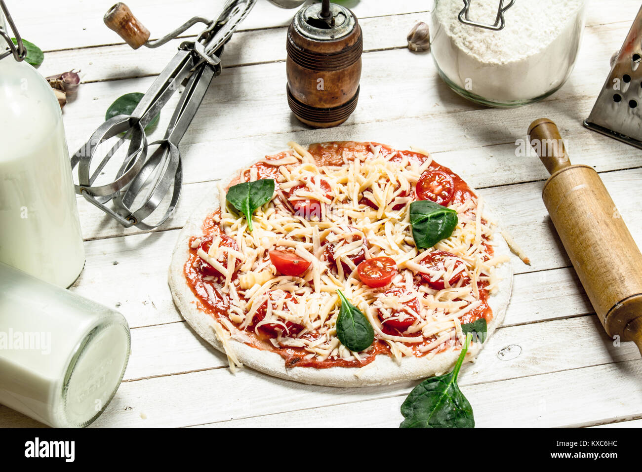 Preparation of pizza with various ingredients. On a white wooden table ...