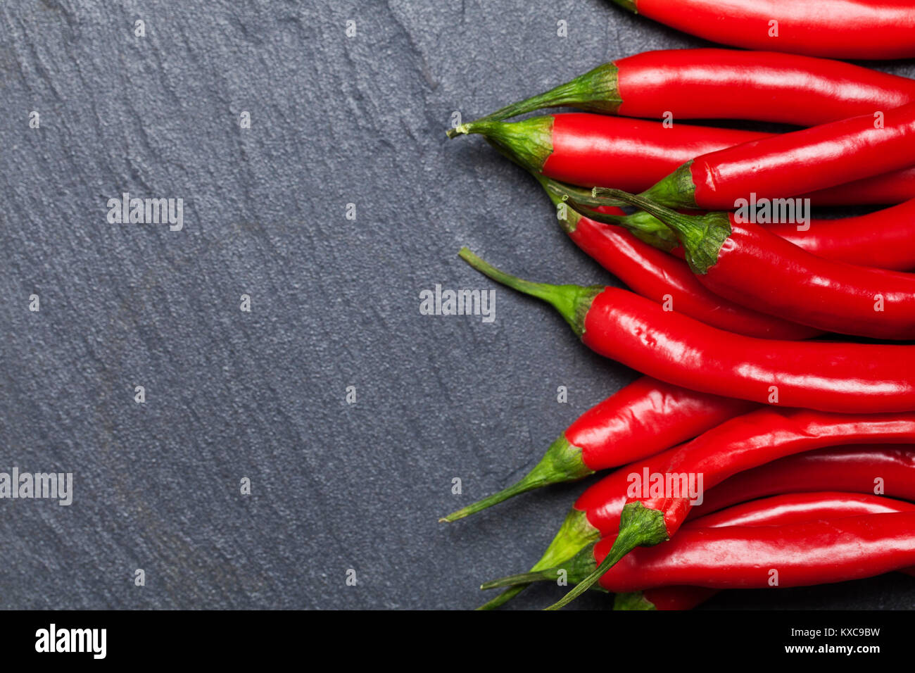 Red fresh chili peppers on a dark slate background Stock Photo - Alamy