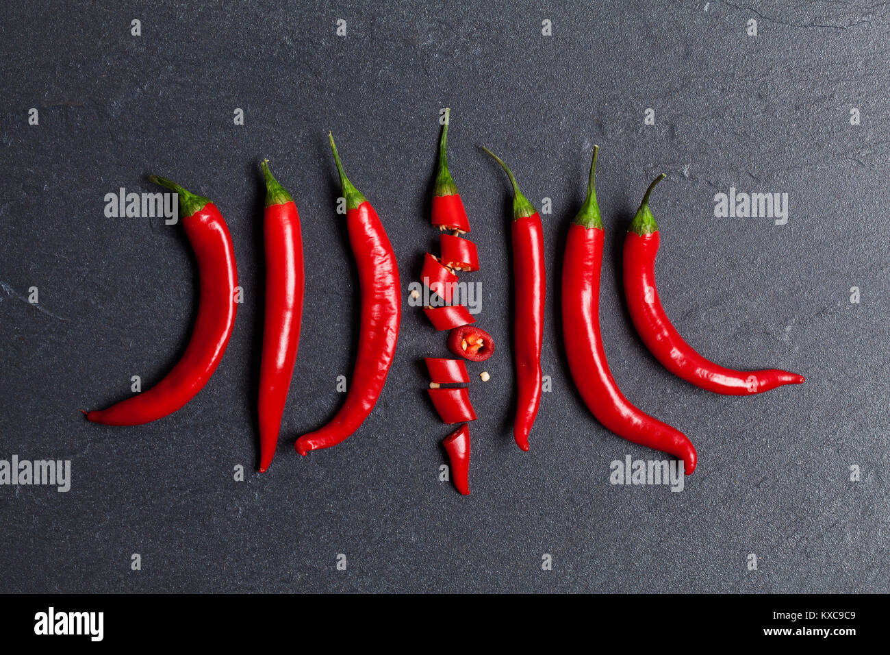 Red fresh chili pepper chopped into pieces on a dark slate background ...