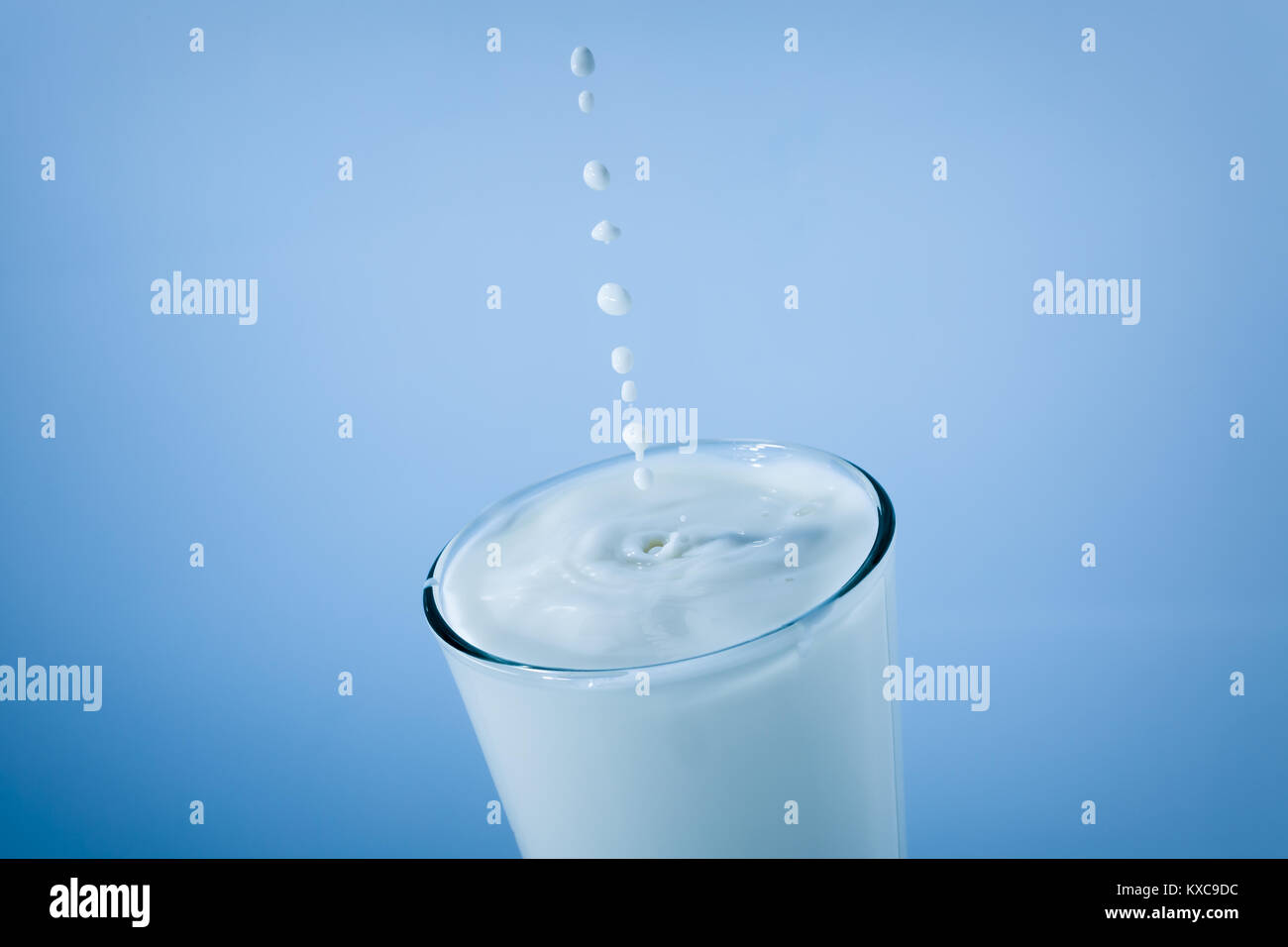 Milk glass with falling drops and splash on blue background, closeup ...