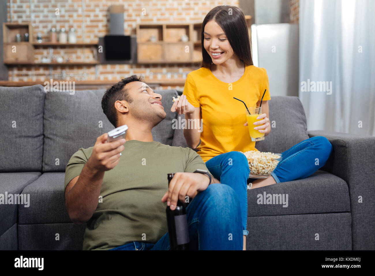 Positive woman offering popcorn to her boyfriend and smiling cheerfully ...