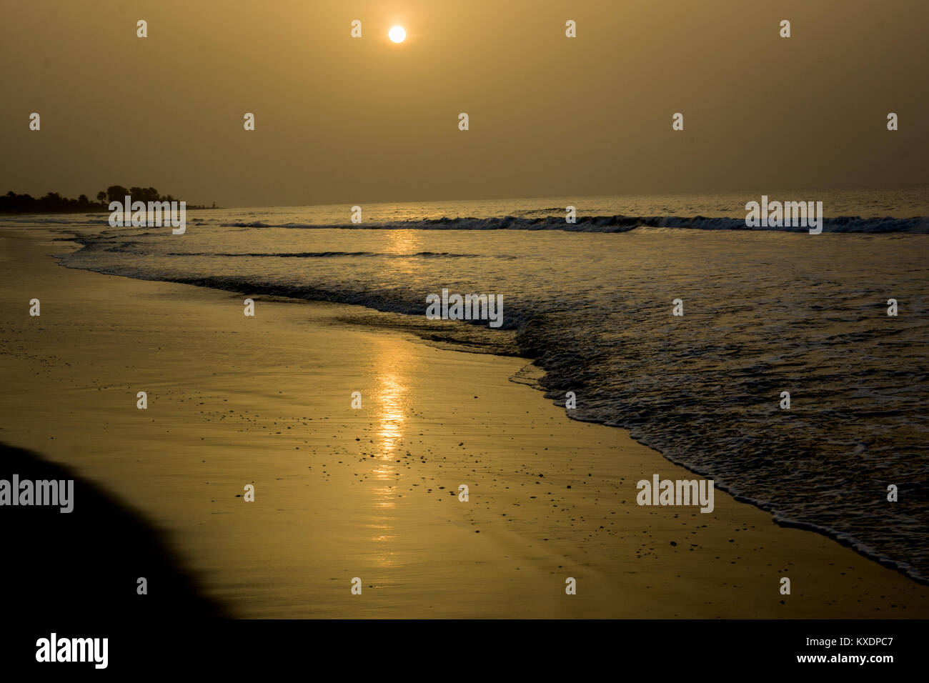A beautiful golden sun sets over Kotu Beach in The Gambia casting a ...