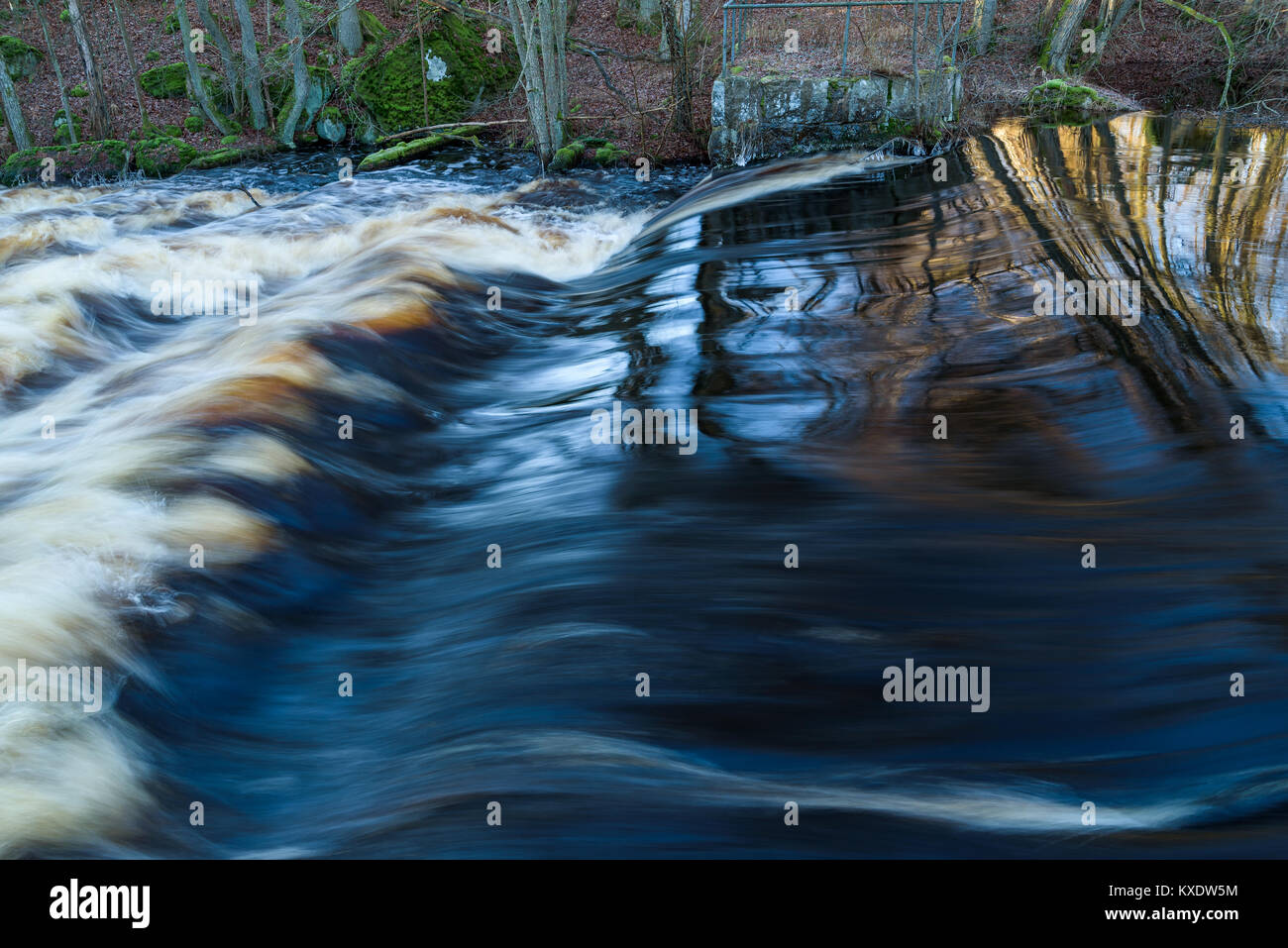 Smooth, abstract flow of river water over submerged manmade structure ...