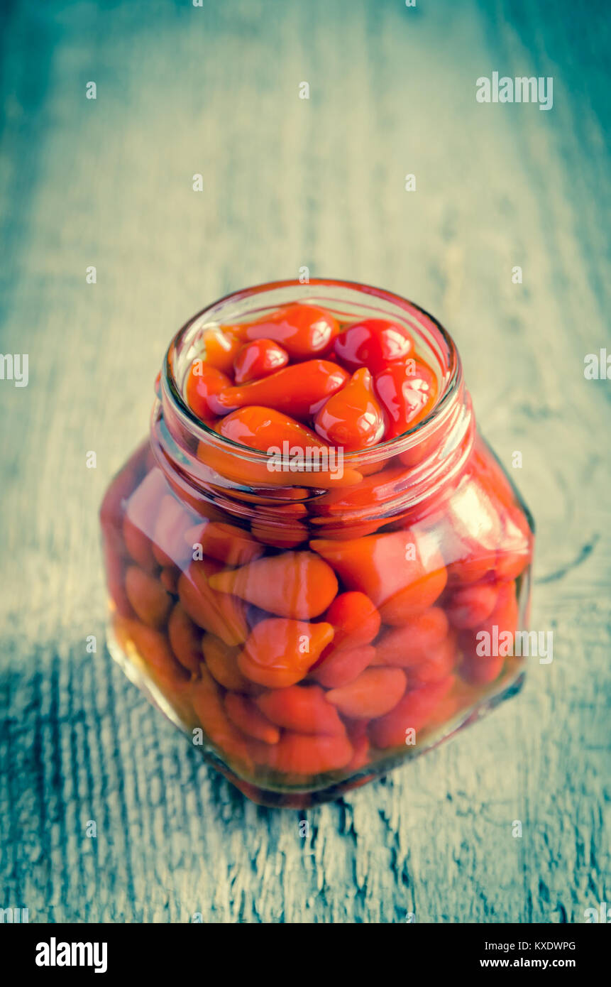Red peppers drops in glass jar on the wooden background Stock Photo - Alamy