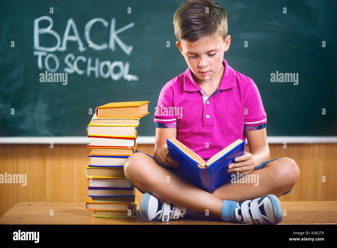 Cute school boy reading book in classroom against blackboard Stock ...