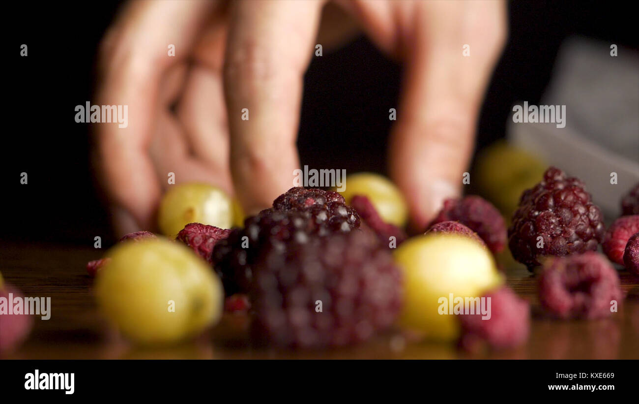 Male hand takes berries and wooden table on black background. Male hand ...