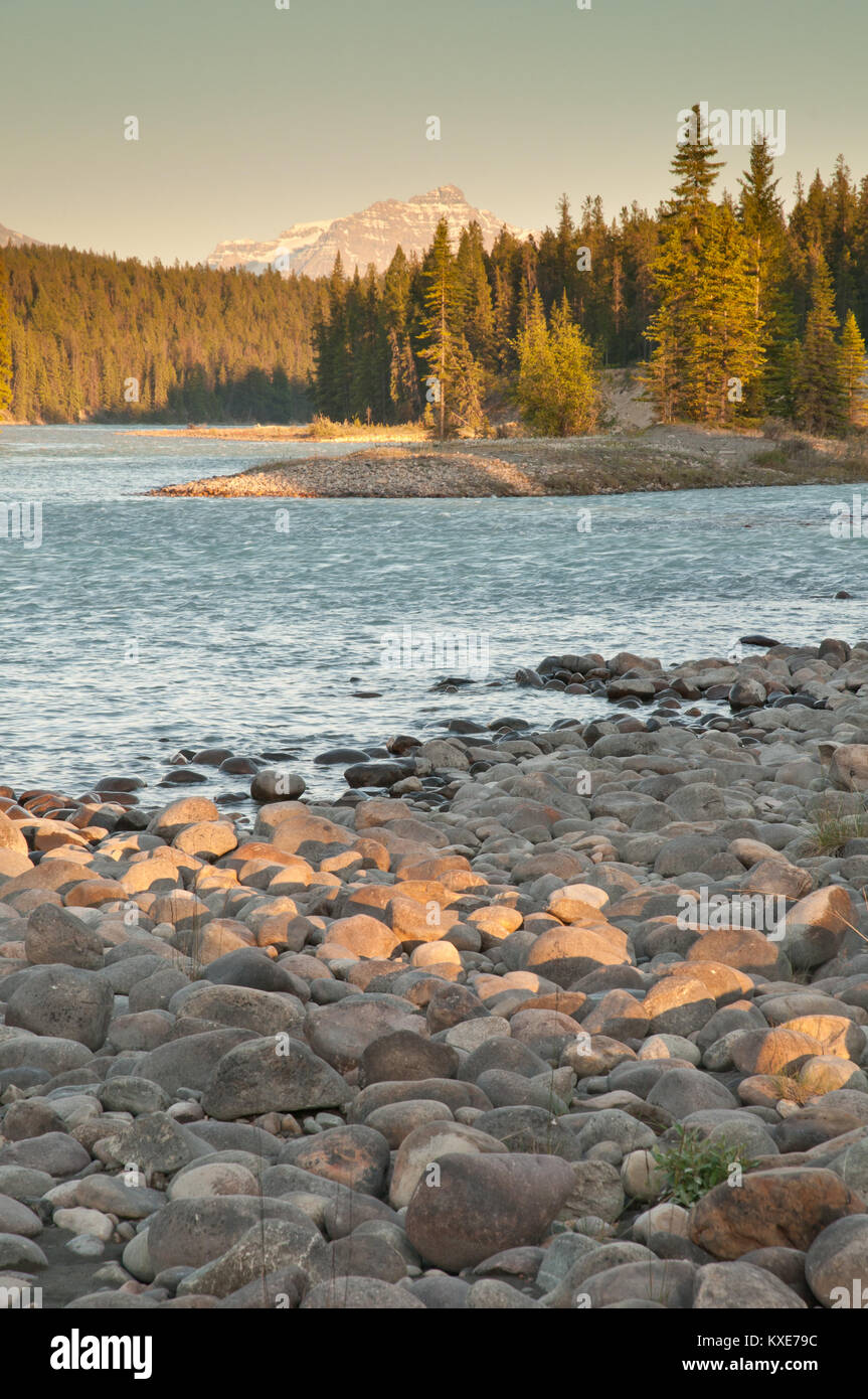 Morning rays shining on pebbles along river bank with mountain in ...