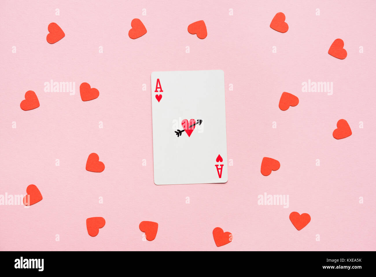 Heart ace of playing card with red hearts lying around on pink surface ...