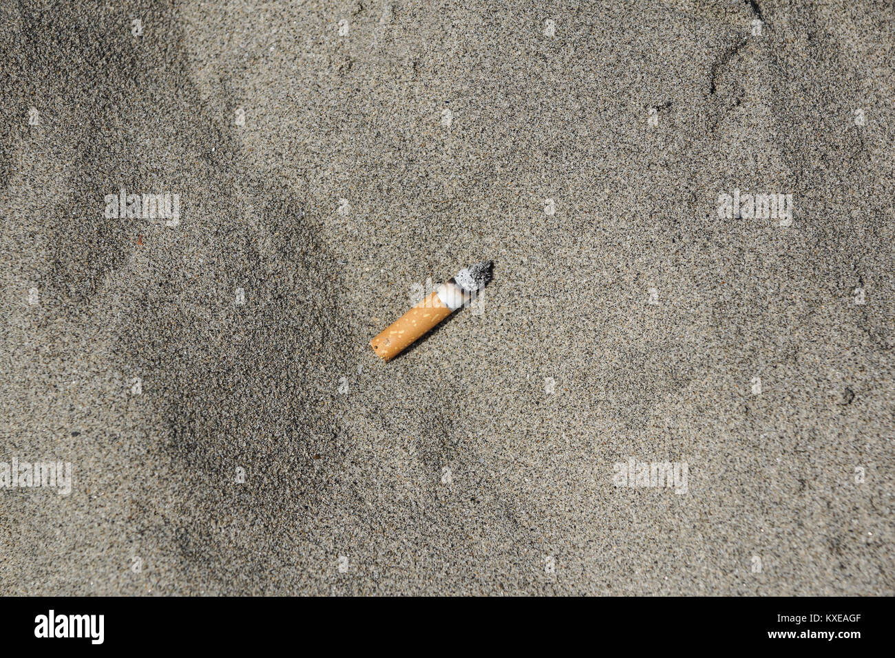 Cigarette on sand beach pollution rubbish Stock Photo - Alamy
