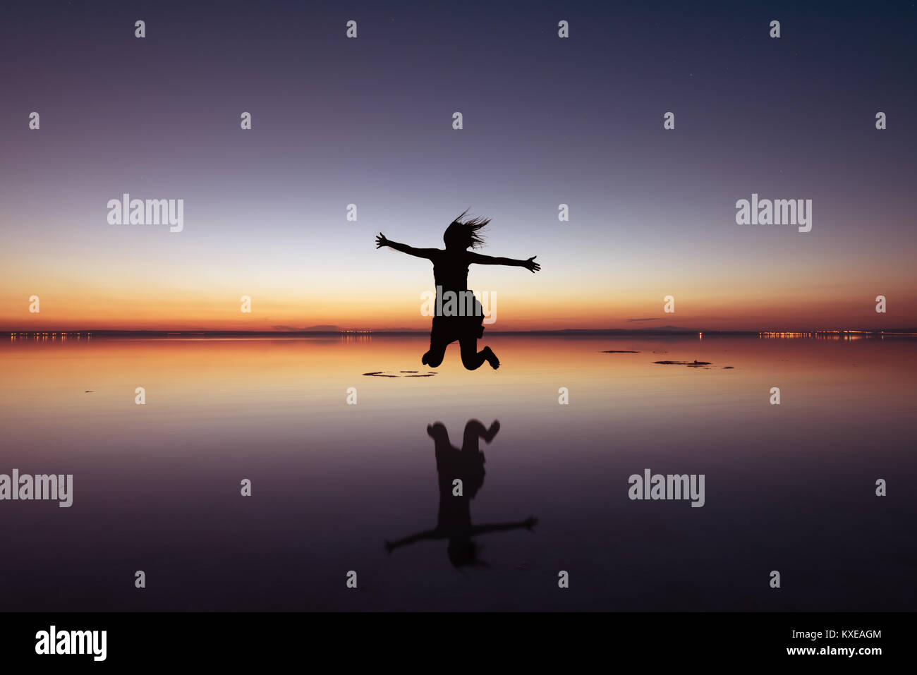 Woman jumping up in a beautiful sunset w,th reflection Stock Photo - Alamy