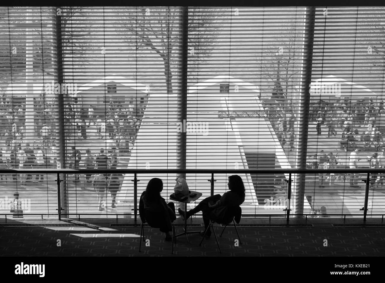 Two people sit by a large window overlooking a large crowd outside the ...