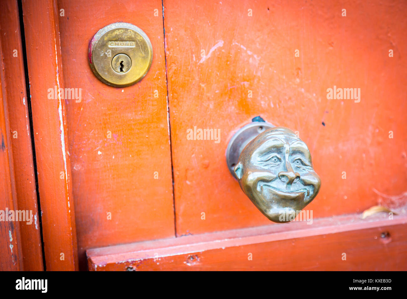 A red door with a distorted face as a knob Stock Photo - Alamy