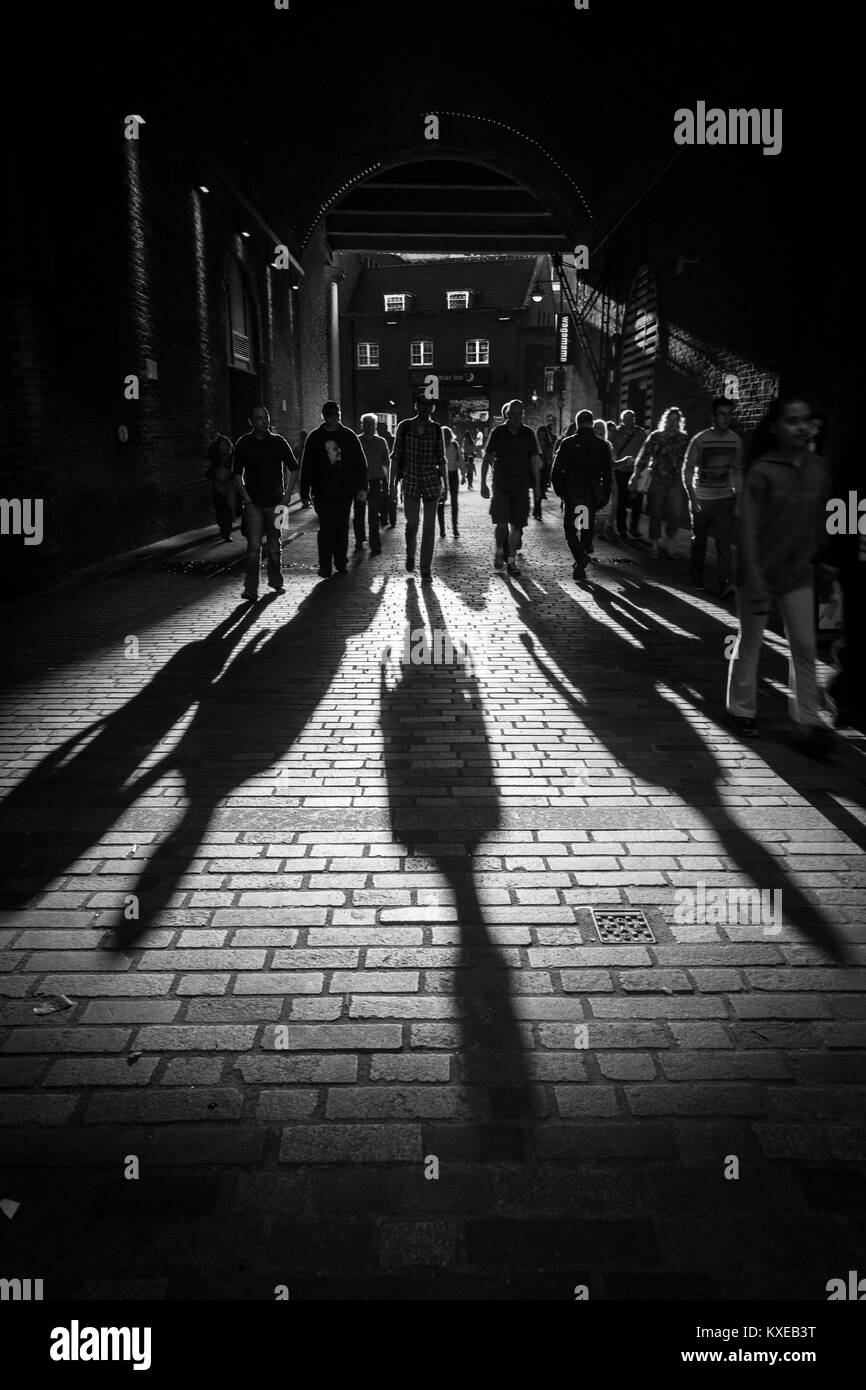 Stretched shadows as a group of people walk into a tunnel with the sun ...
