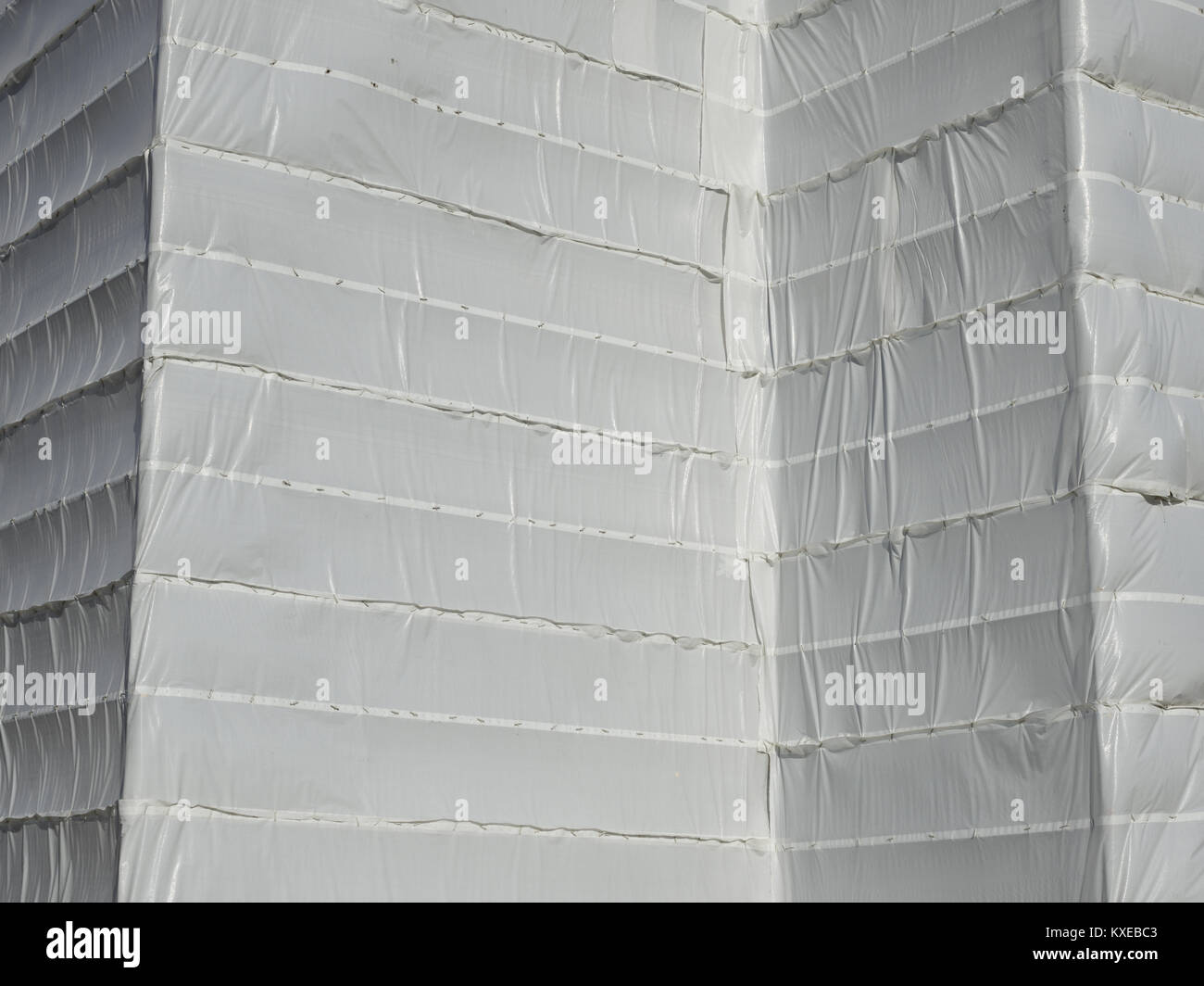 A tall building under renovation is wrapped in white plastic sheeting ...