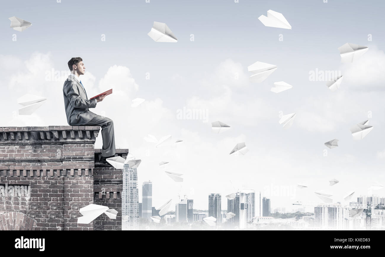 Man on roof edge reading book and cityscape at background Stock Photo ...